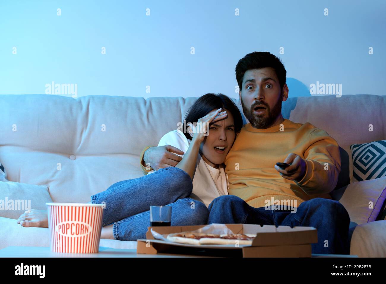 Frightened couple watching TV with popcorn and pizza on sofa Stock ...