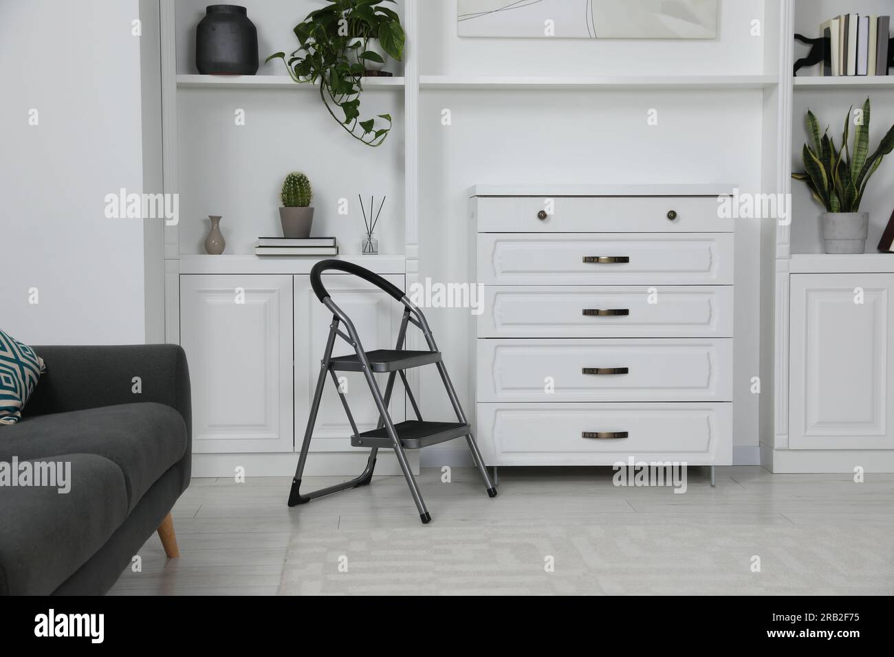 Metal folding ladder near chest of drawers and shelves with accessories ...