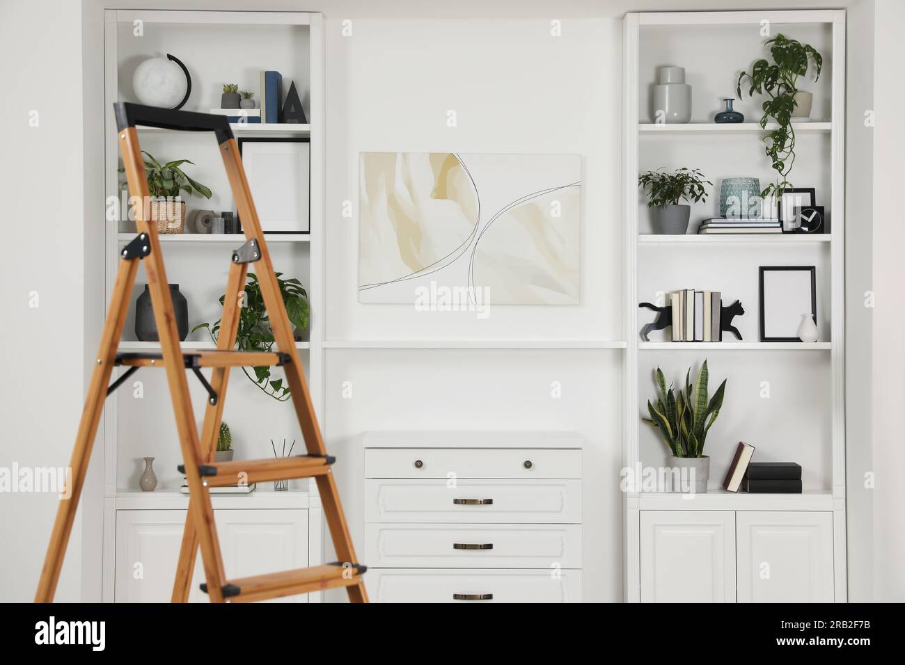 Wooden folding ladder near chest of drawers and shelves with ...