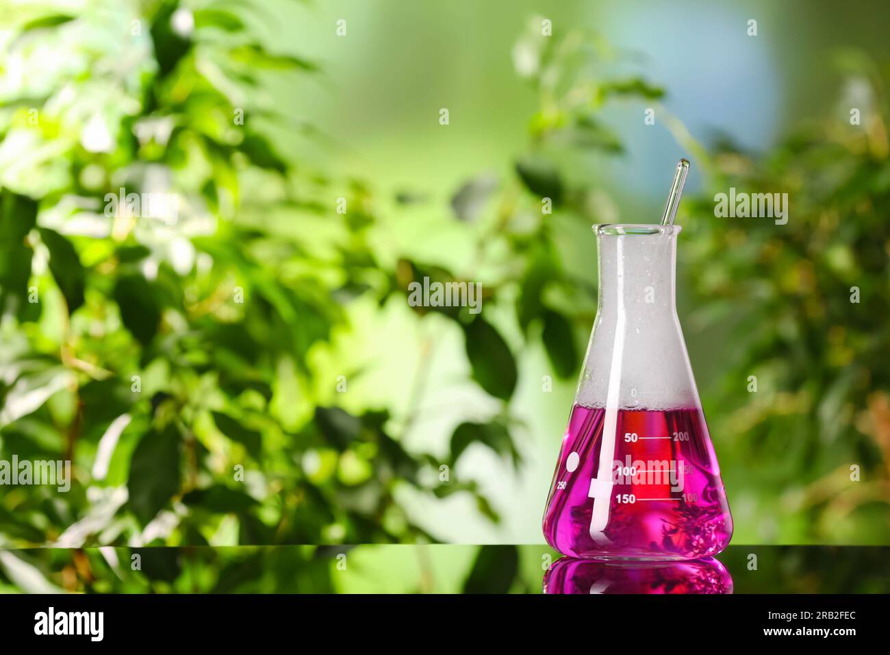 Laboratory flask with colorful liquid on glass table outdoors, space ...