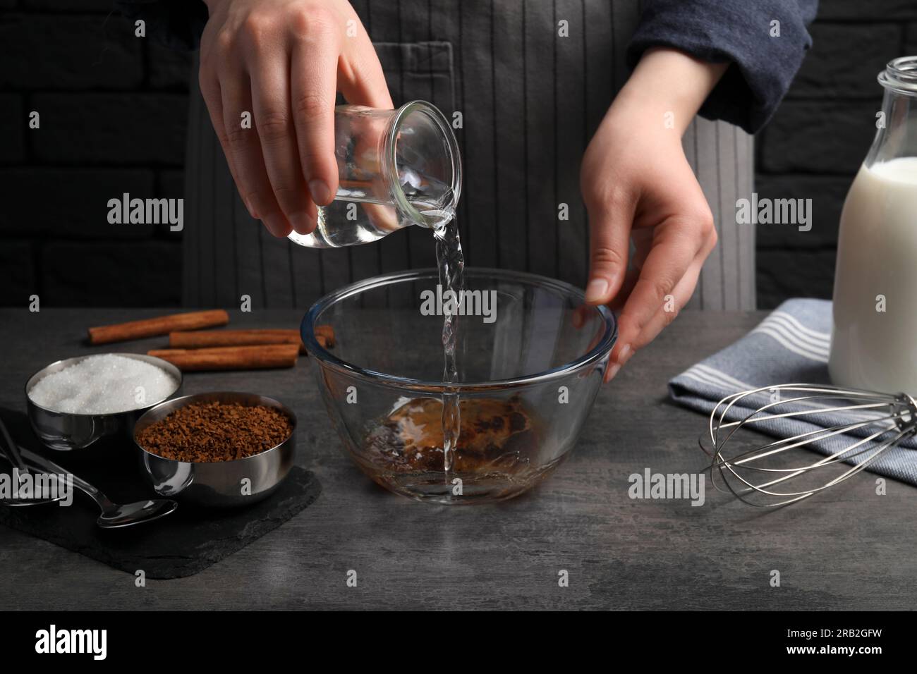 Making dalgona coffee. Woman pouring water into bowl at grey table ...