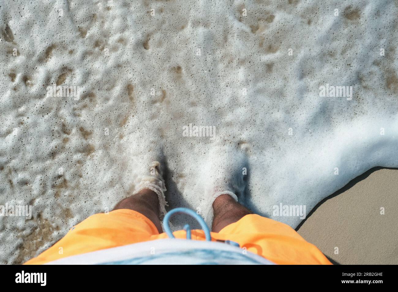 In summer orange swimsuit waves washing over feet of man at beach Stock ...