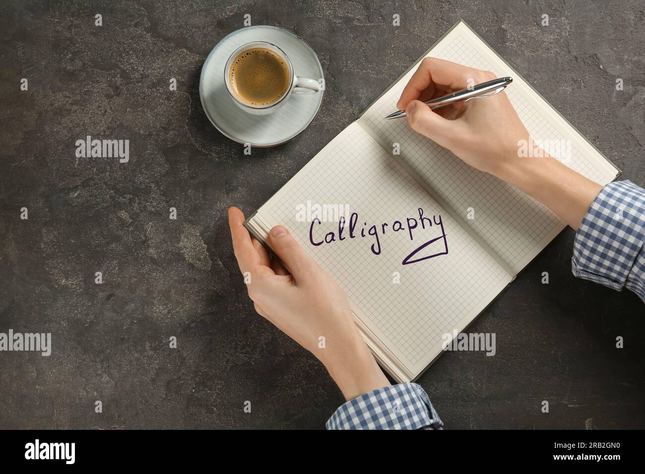 Woman writing word Calligraphy in notebook at grey table, top view ...