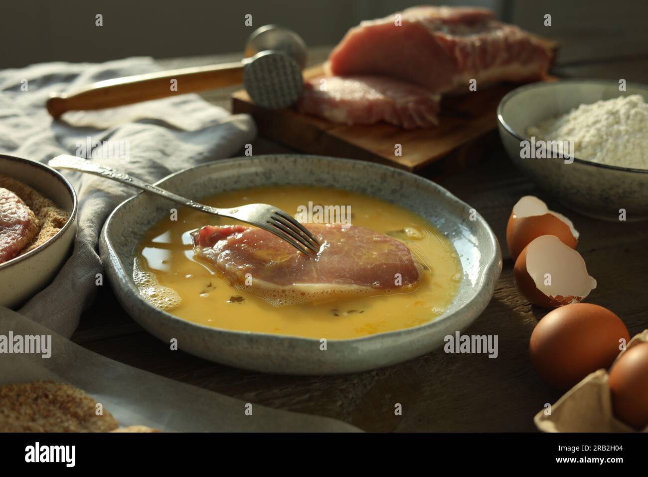 Cooking schnitzel. Raw pork chop in eggs, meat mallet and ingredients ...