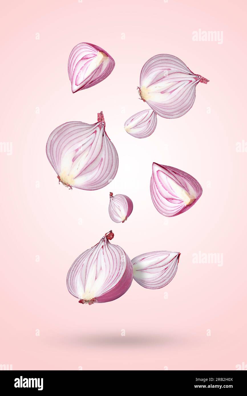 Cut red onions falling on light pink background Stock Photo - Alamy