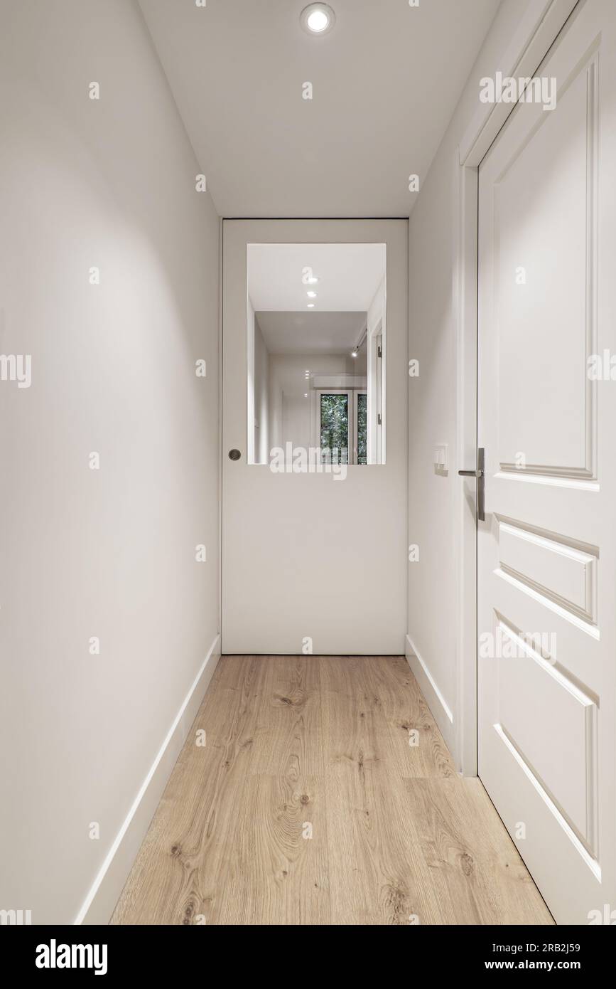 A long corridor of a house with a light wooden floor with access doors ...