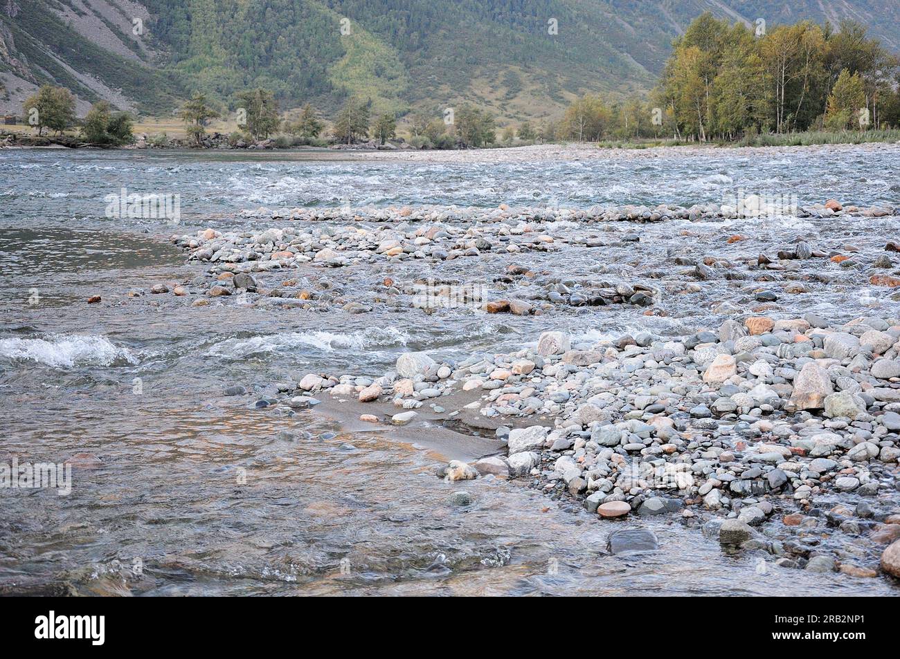 Rocky banks of a shallow but wide river flowing through a mountain ...