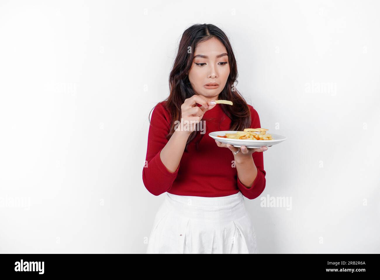 Young disgusted woman in casual sweater is holding fast food french ...