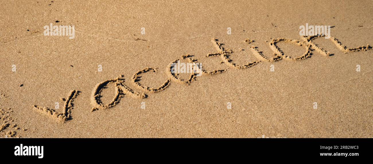 Text VACATION handwritten in sand surface. Blue ocean wave washing away ...