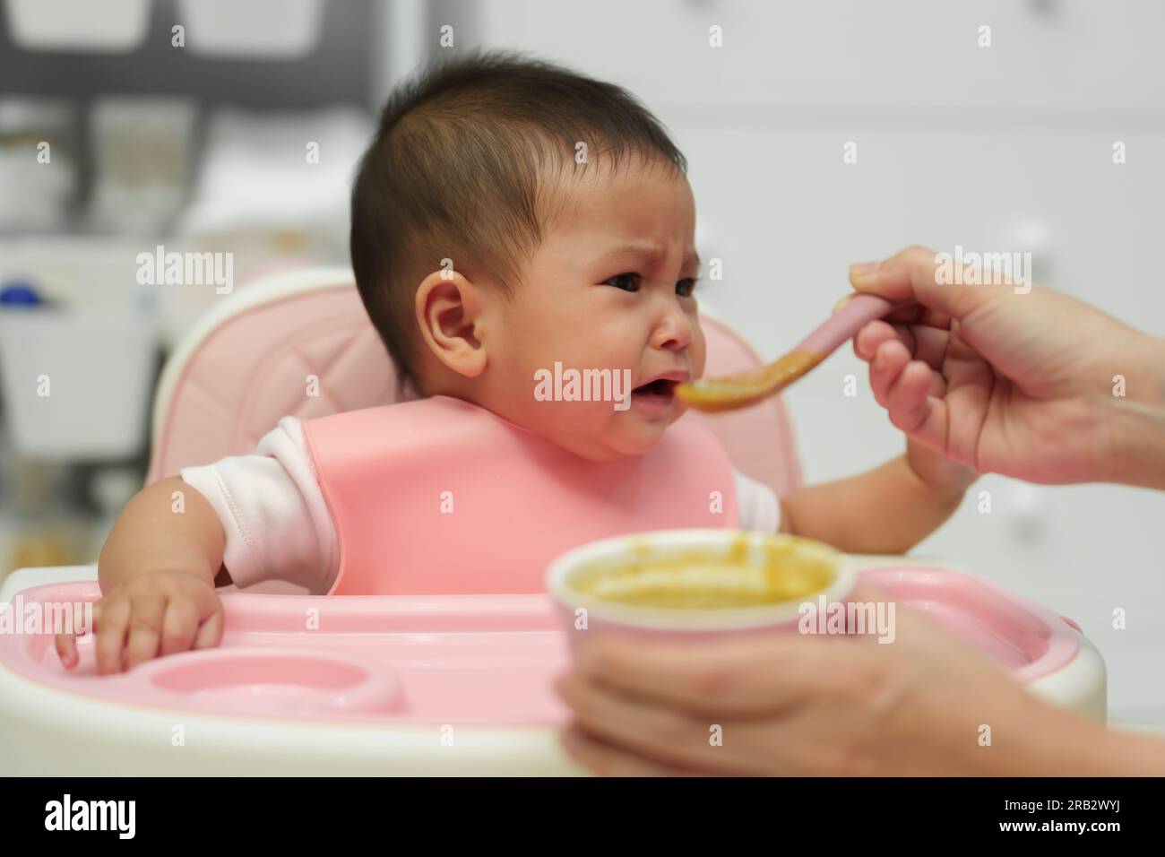 mother feeding food to her crying infant baby with a spoon, refuse to ...