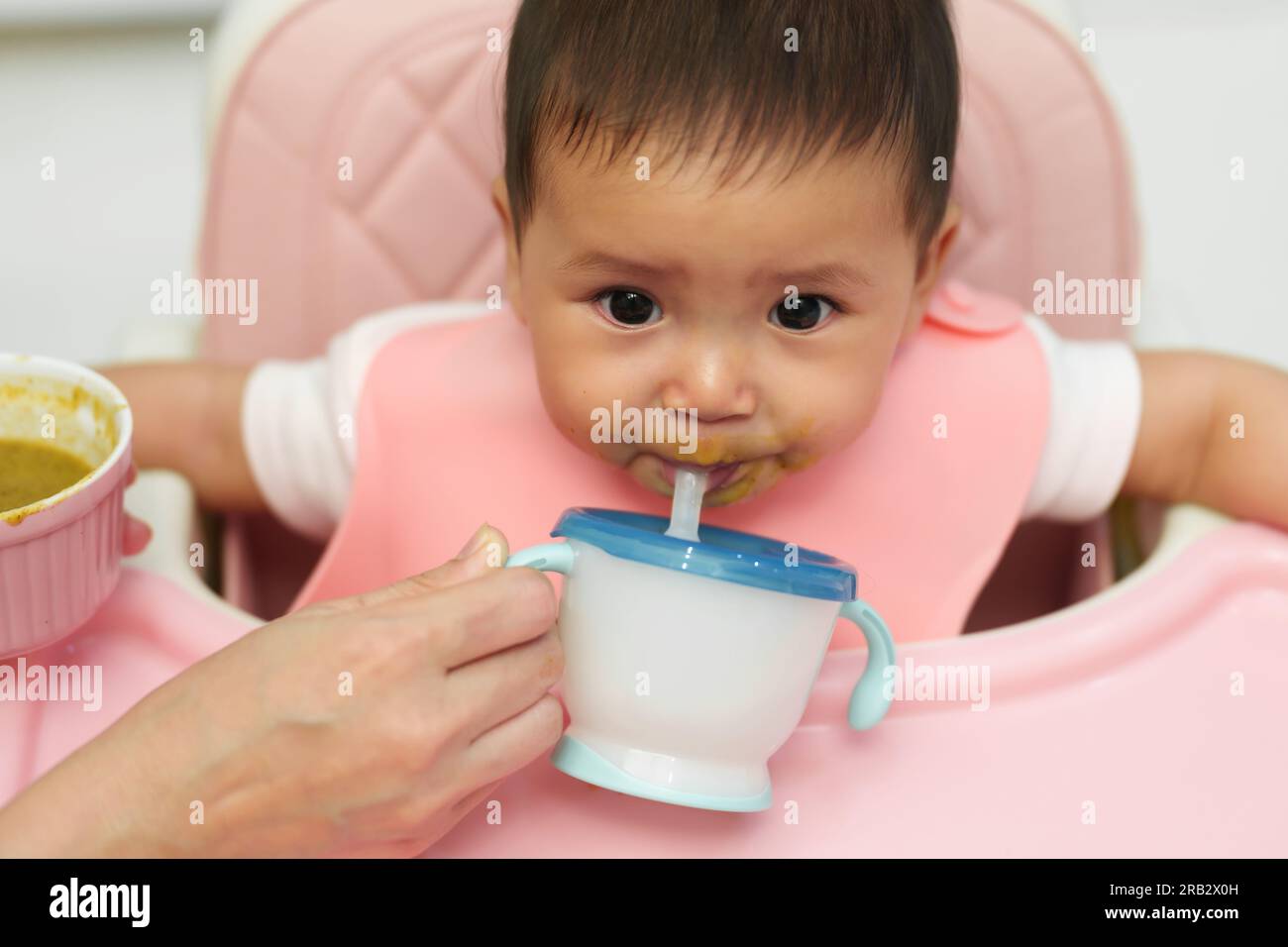 infant baby drinking a glass of water with a straw by mother feeding ...
