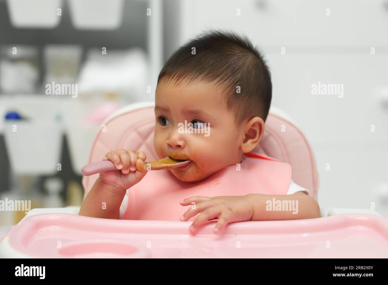 happy infant baby eating food itself with a spoon at home Stock Photo ...