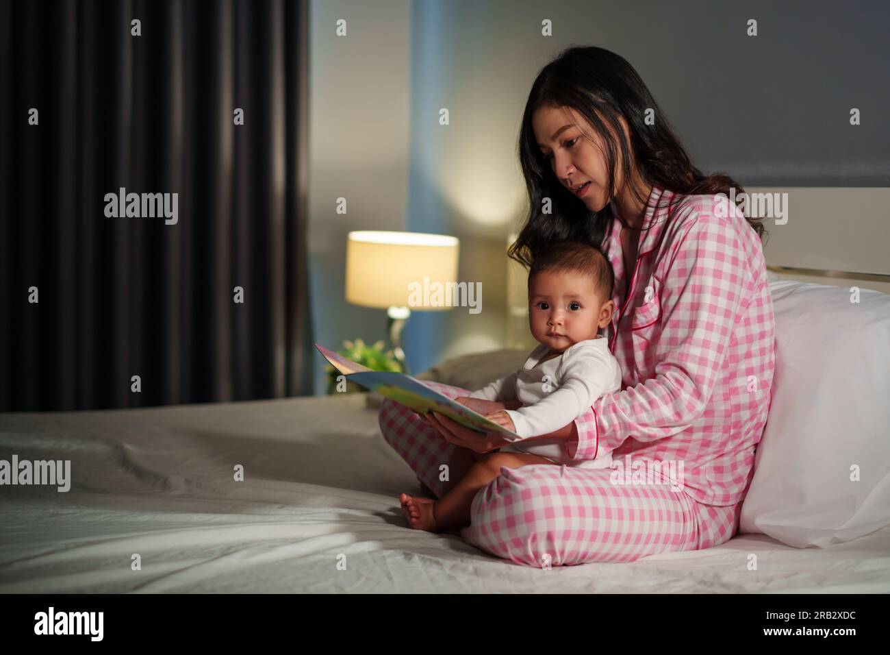 mother read story in the book for infant baby on a bed at night Stock ...
