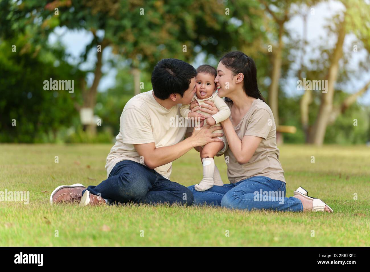 happy family sitting on a green grass filed. father and mother kissing ...