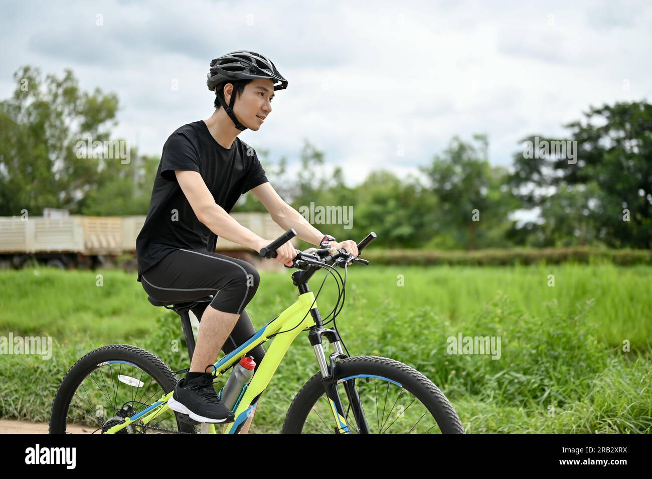 A happy and healthy-fit Asian man in sportswear and a bike helmet rides ...