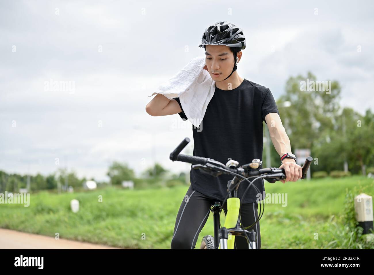 A tired and sweaty young Asian man in sportswear and a bike helmet ...