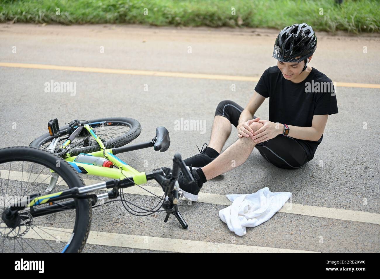 An injured young Asian male cyclist in sportswear and a bike helmet ...