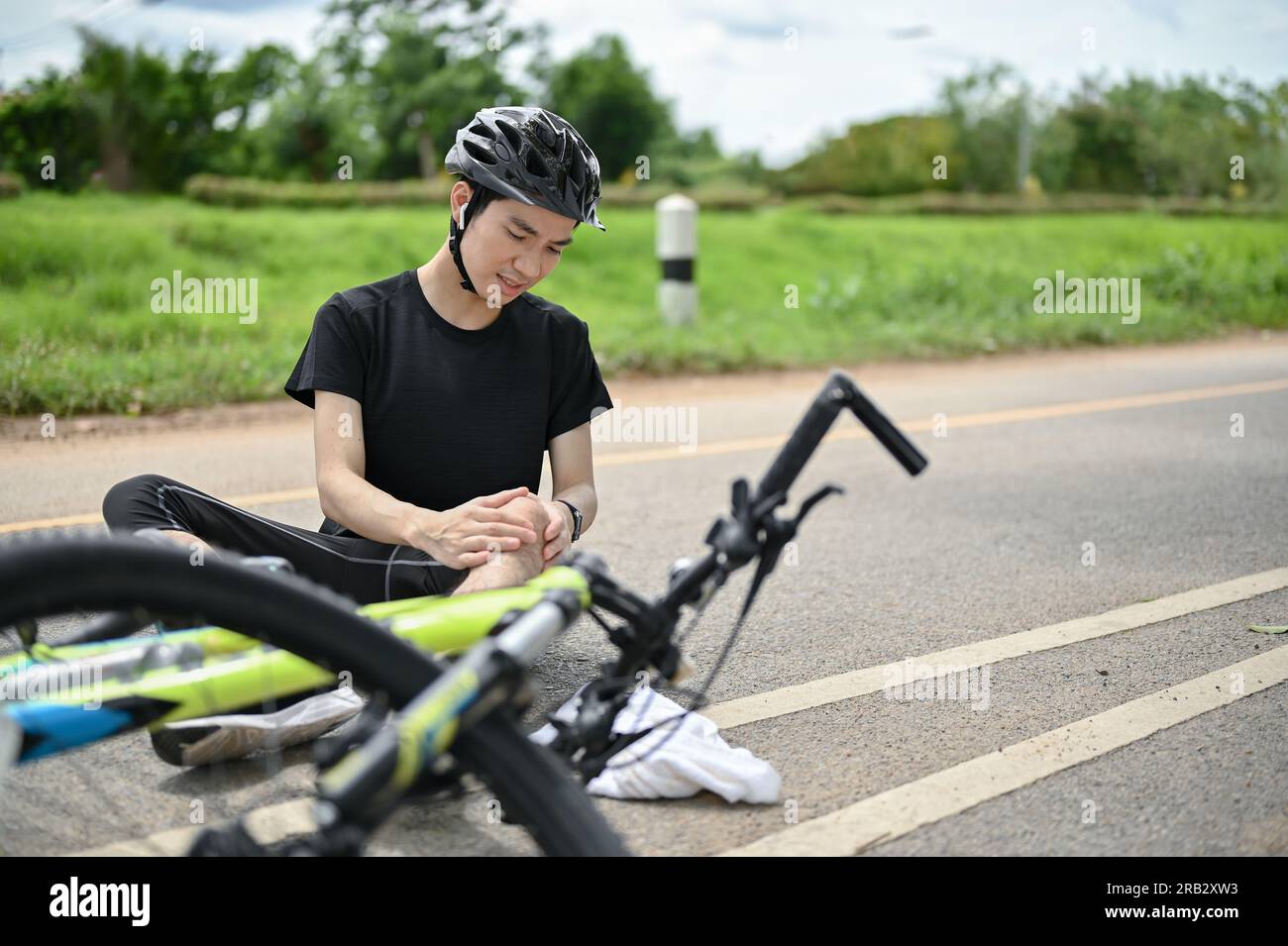An injured young Asian male cyclist in sportswear and a bike helmet ...