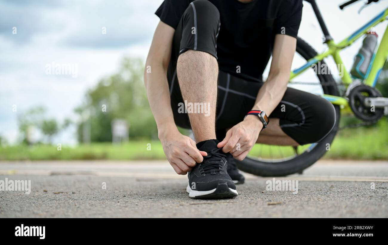 Cropped image of a healthy, fit male cyclist tying his shoelaces before ...