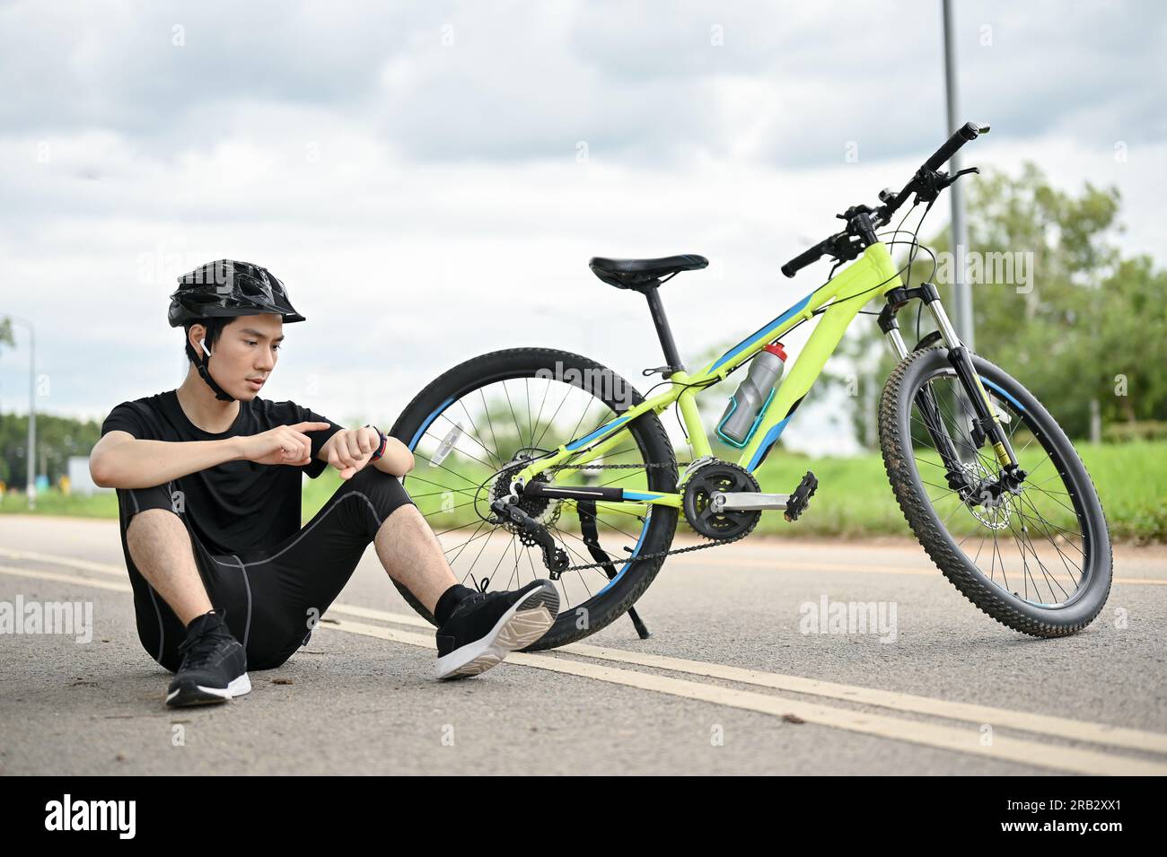 A tired young Asian male cyclist sitting on the street with his bike ...