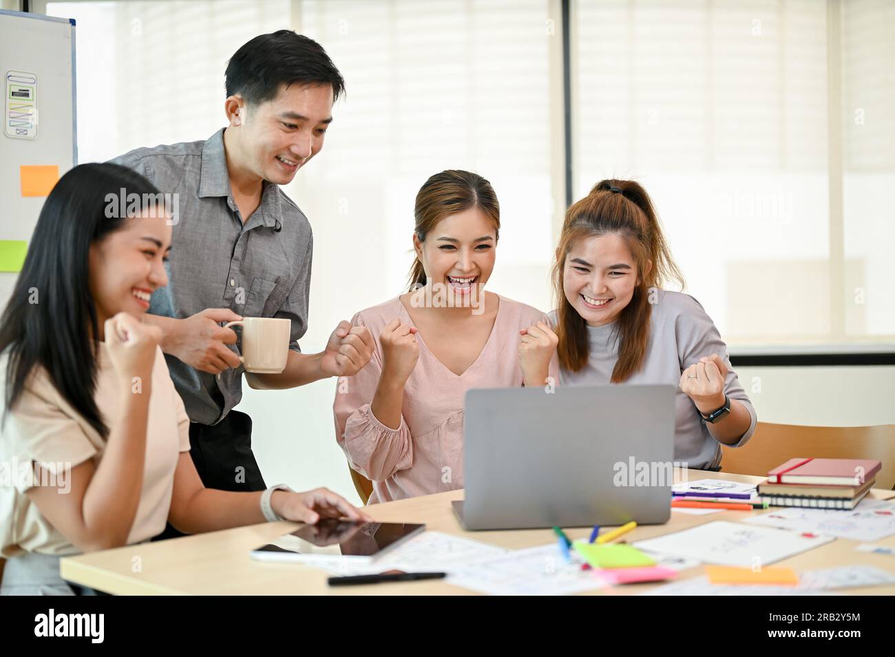 A group of cheerful Asian tech developers looking at a laptop screen ...