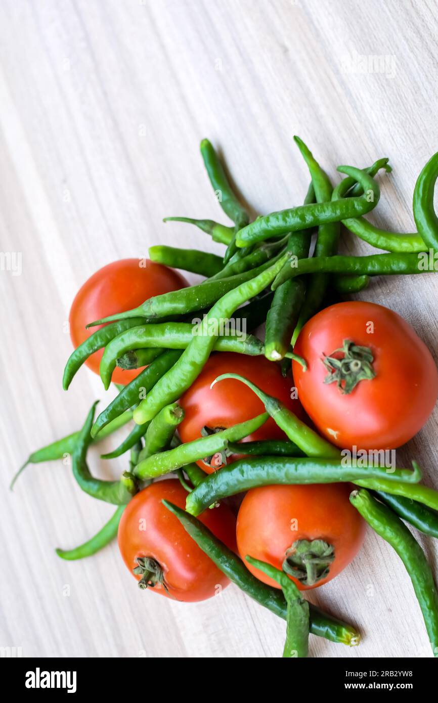 Red tomato and green chili pepper on plain wooden table, green ...