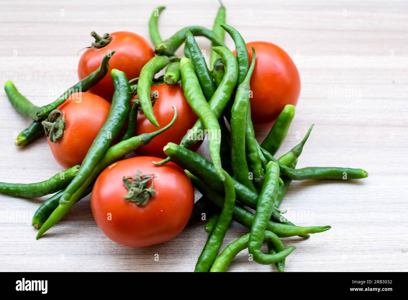 Red tomato and green chili pepper on plain wooden table, green ...