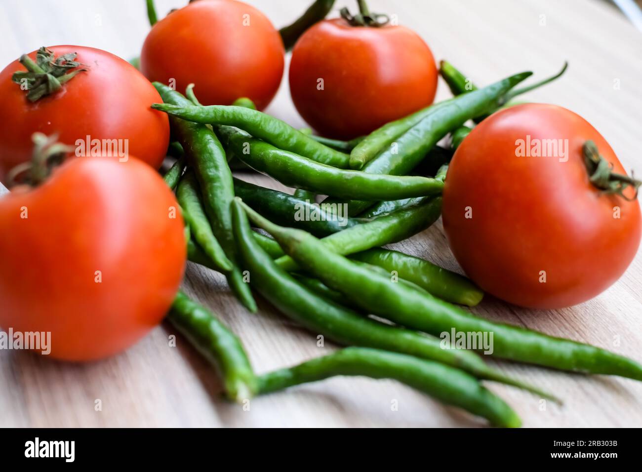 Red tomato and green chili pepper on plain wooden table, green ...