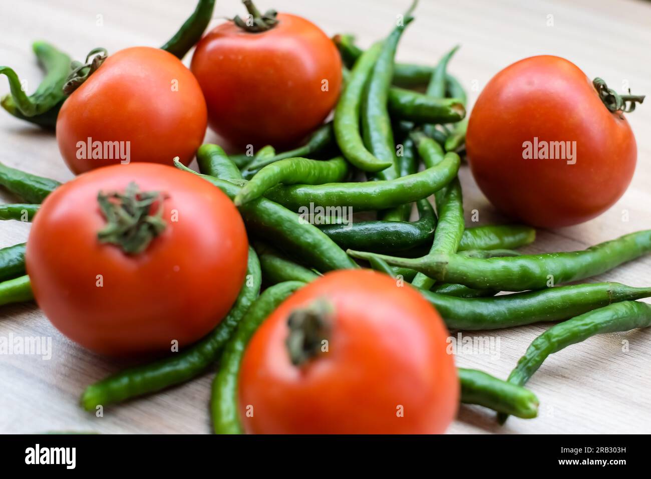 Red tomato and green chili pepper on plain wooden table, green ...