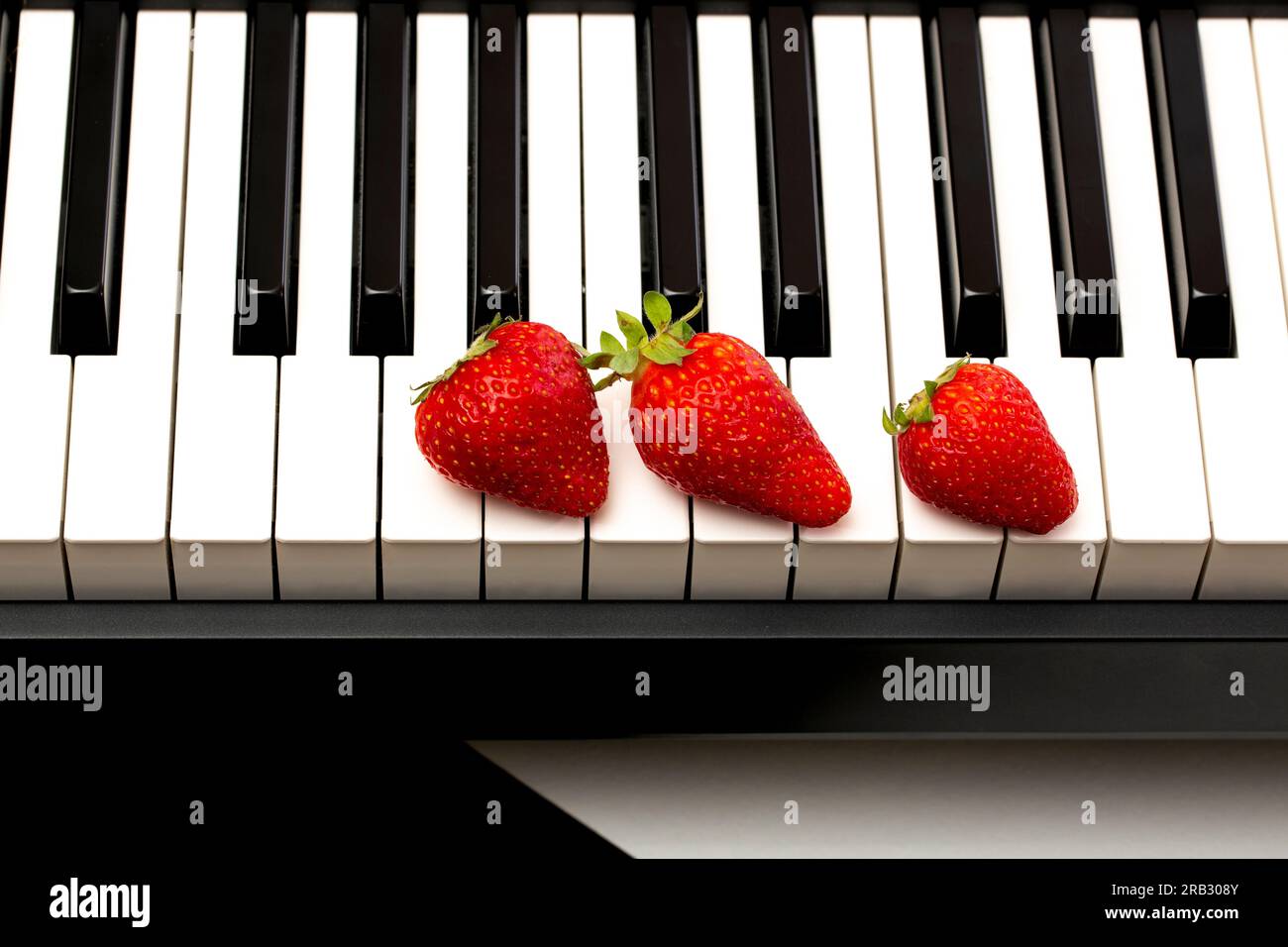 Three ripe strawberries on the piano keys Stock Photo - Alamy