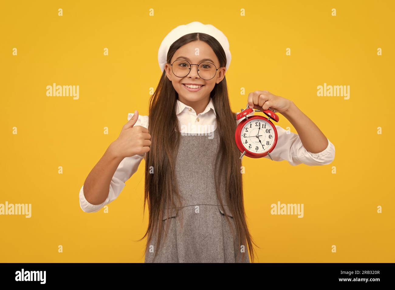 Teenager child hold clock isolated on yellow studio background ...