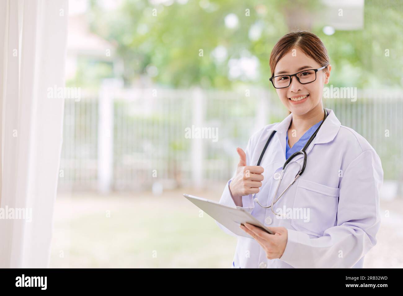 portrait asian young teen medical staff doctor physician thumbs up with green nature blur ...
