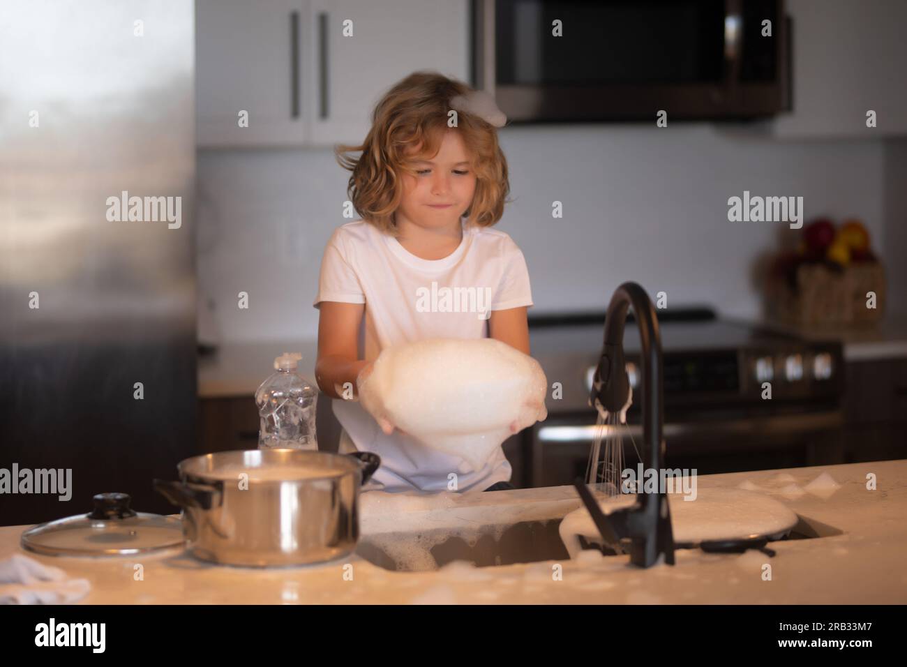 Kid boy washing dishes in the kitchen interior. Child helping his ...