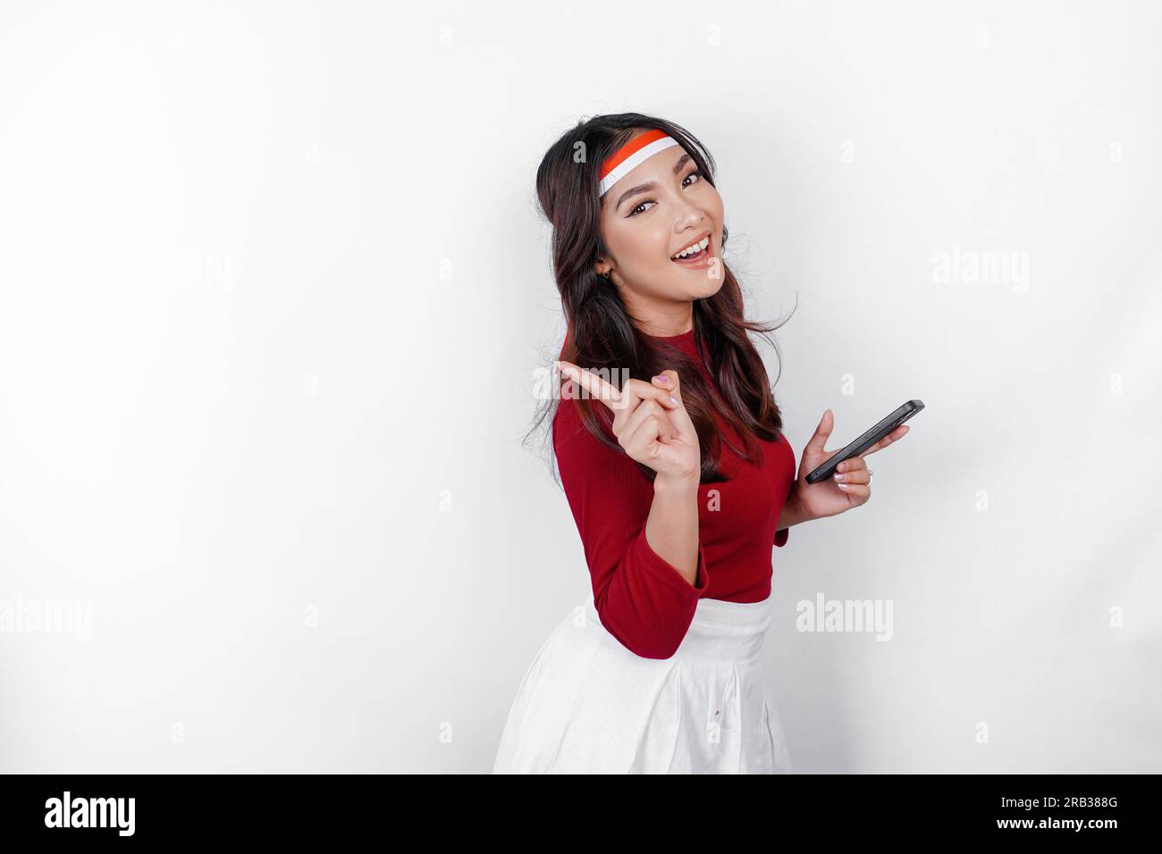 A Happy Asian Woman Wearing Headband Holding Her Phone And Pointing