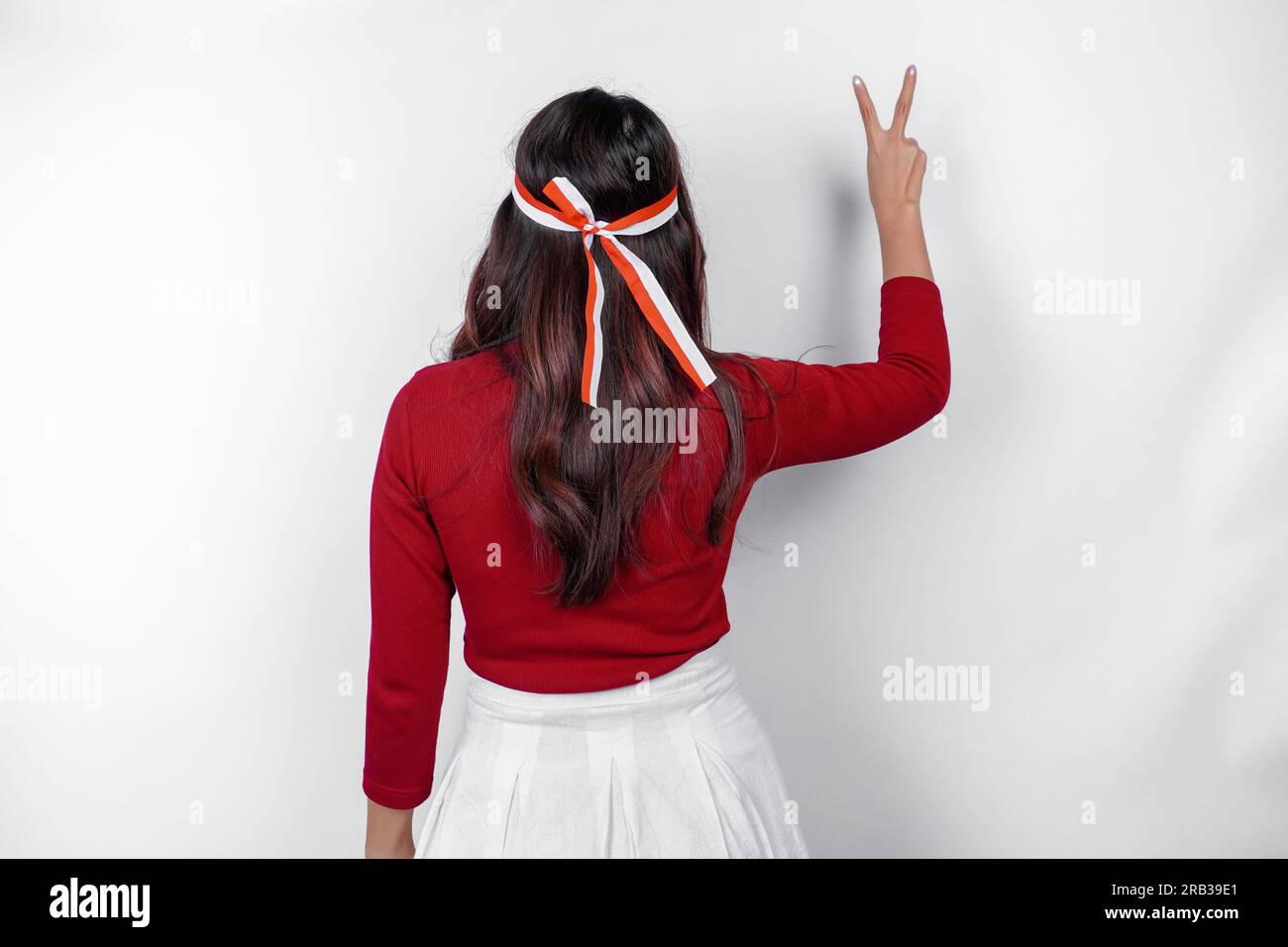 Back view of a young Asian woman wearing a red top expressing peace ...