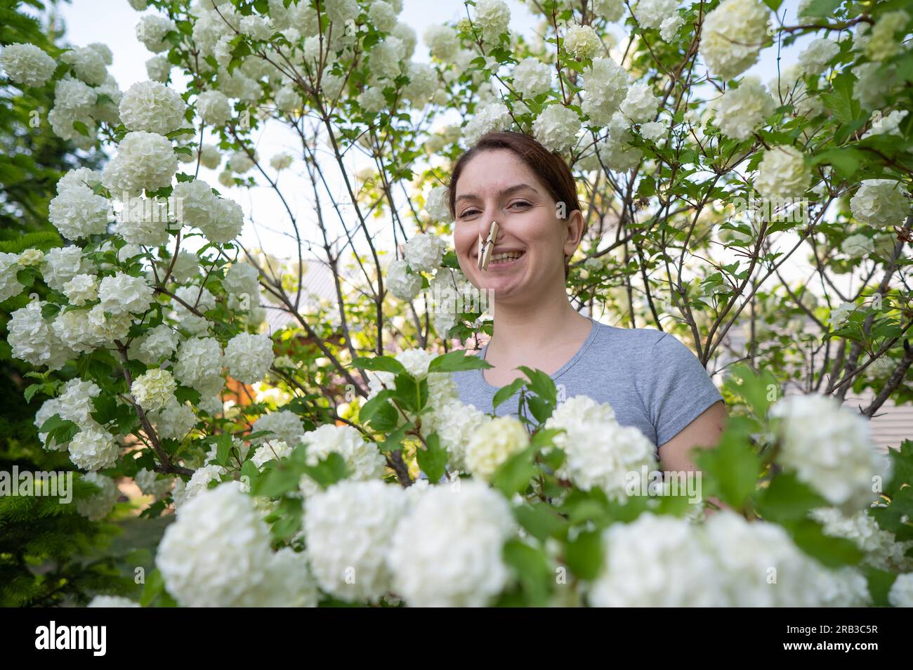 Happy woman with a clothespin on her nose on a walk in a blooming park ...