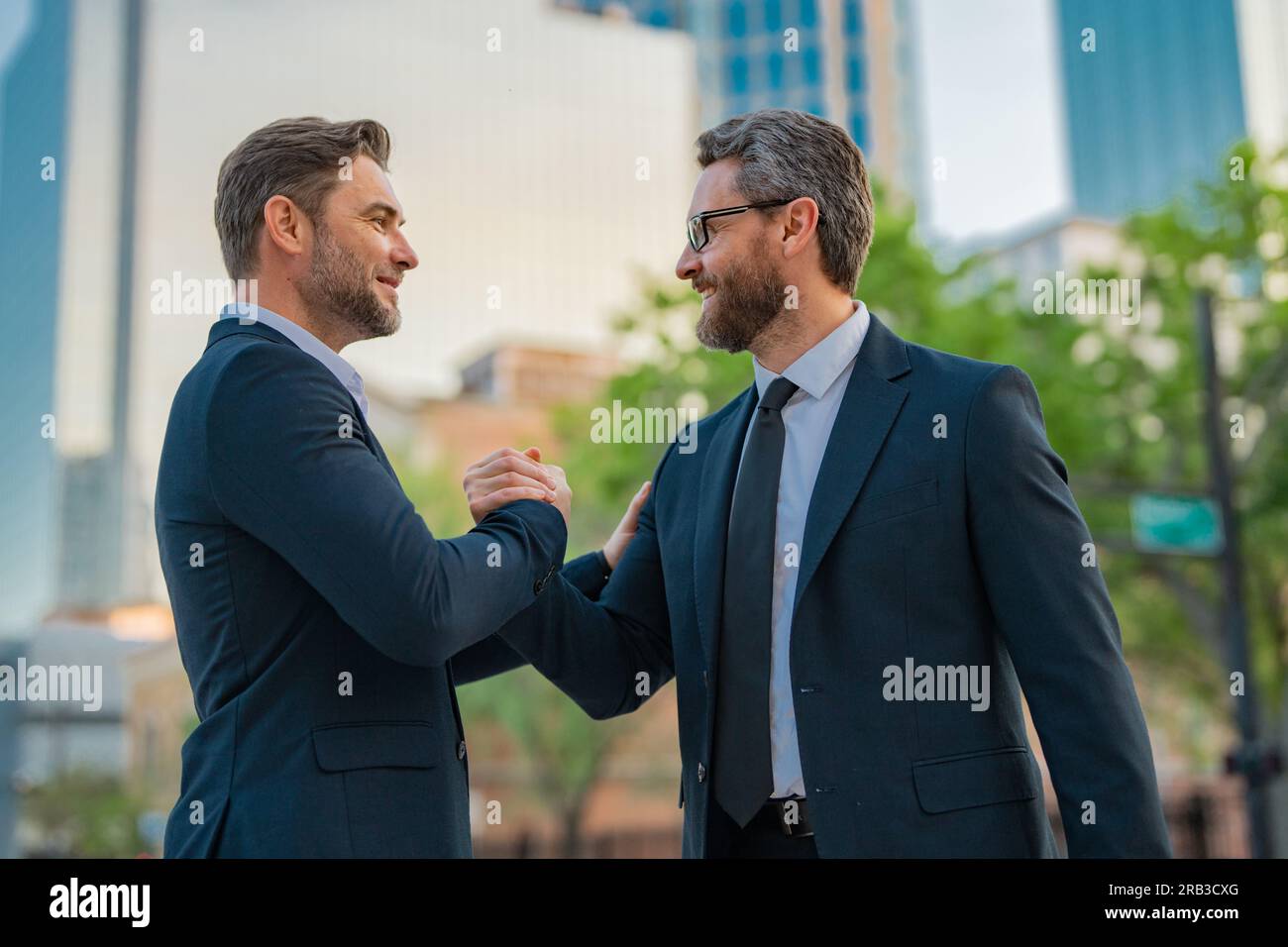 Two businessmen shaking hands on city street. Business men in suit ...