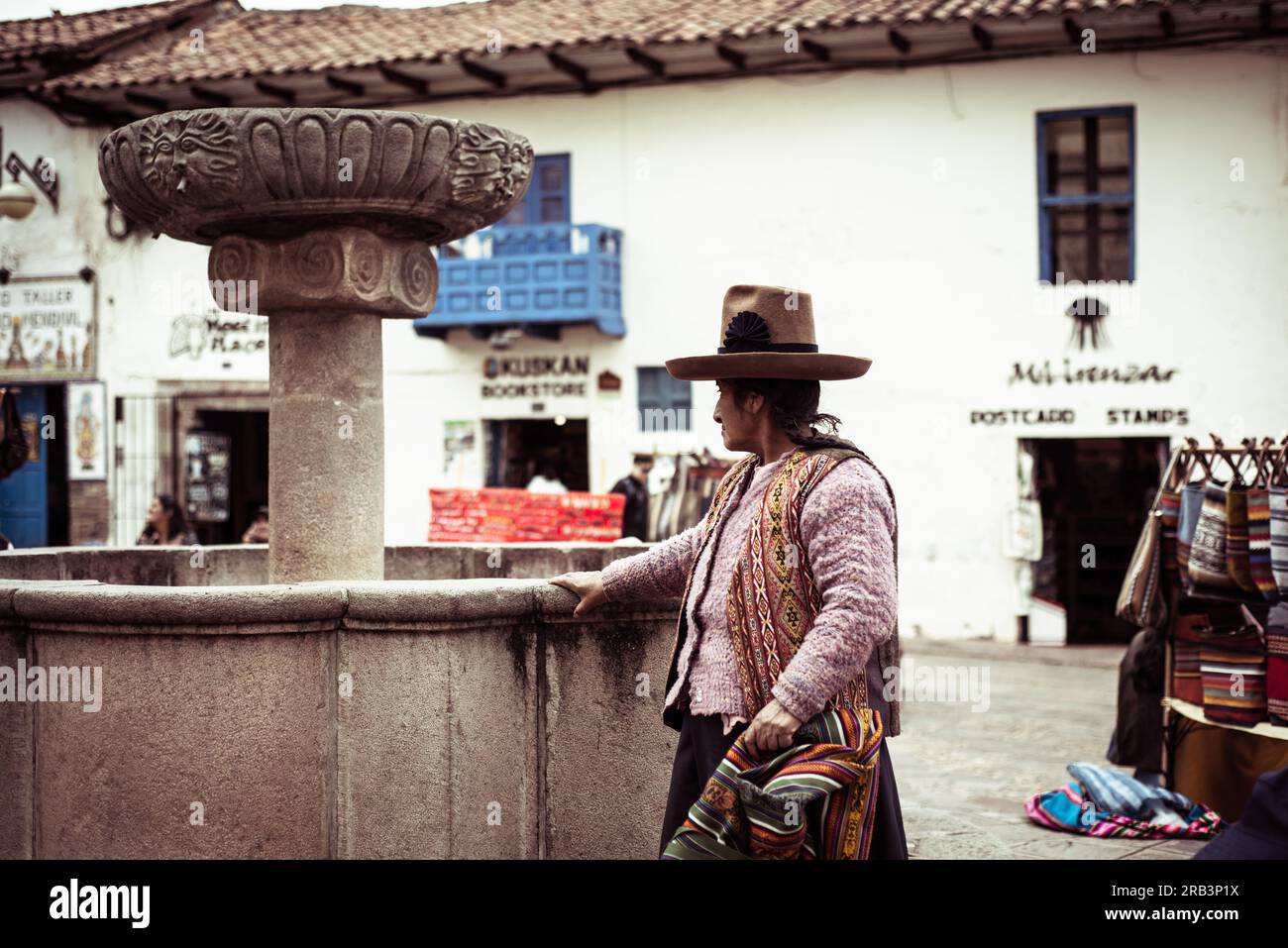 Local Peruvian woman stands in crafts market square with inca building ...