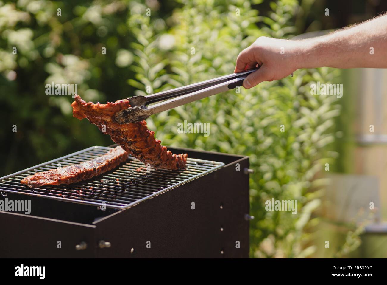 man roasting meat on the grill in the summer garden behind the house ...