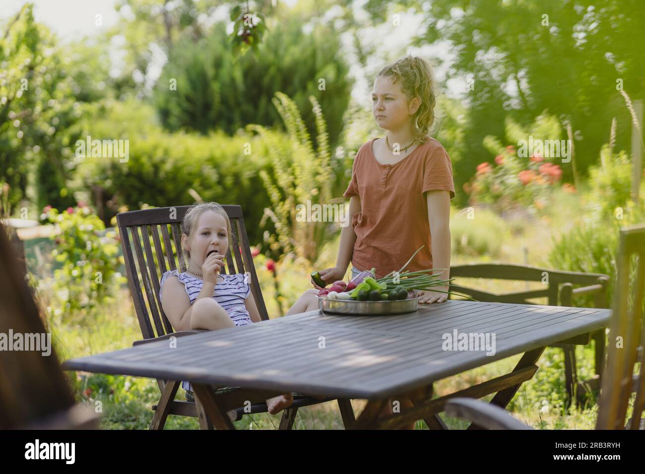 two girls in the summer garden behind the house eating vegetables Stock ...