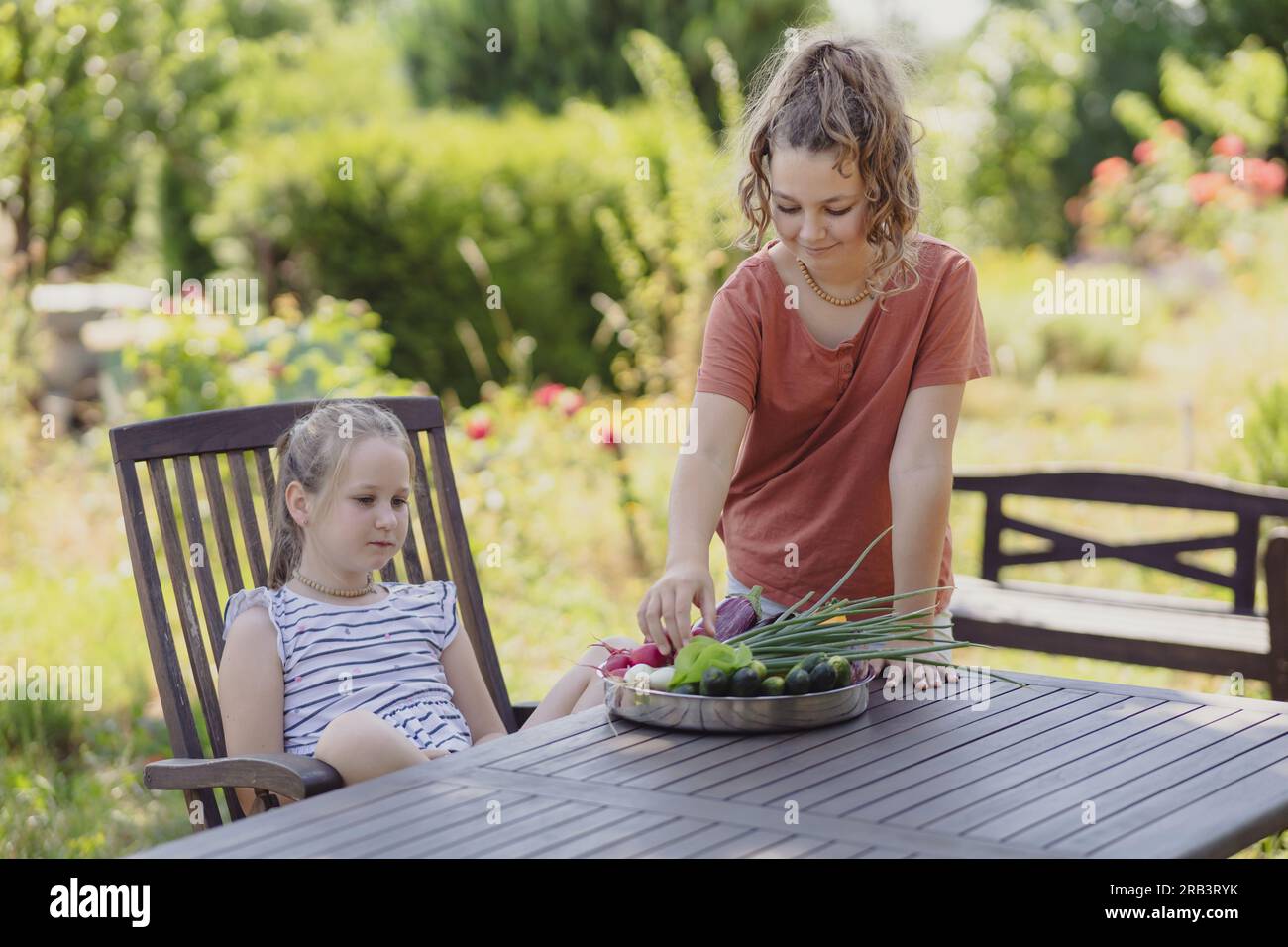 two girls in the summer garden behind the house eating vegetables Stock ...