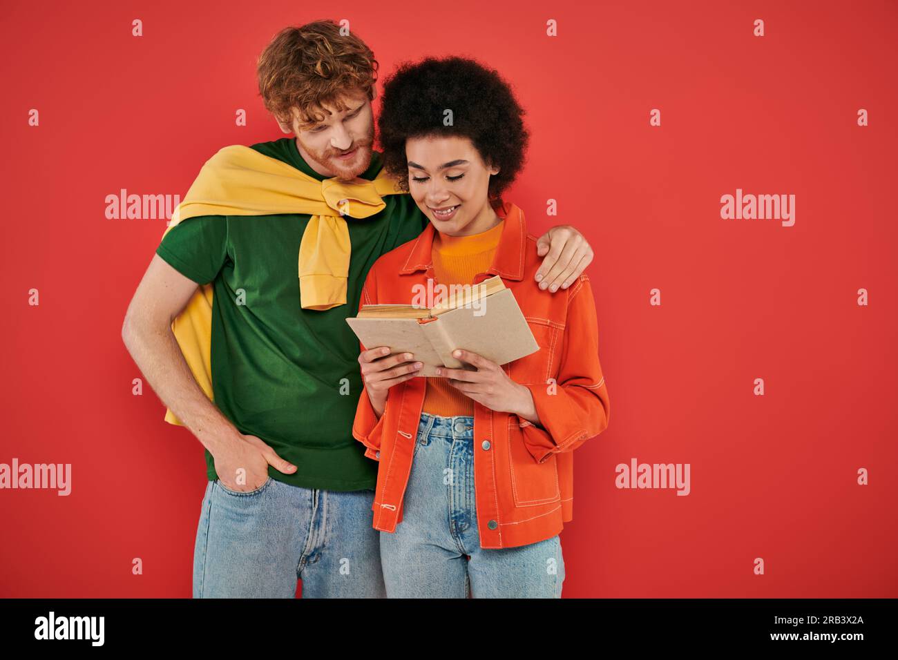 interracial couple hugging and reading book on coral background ...