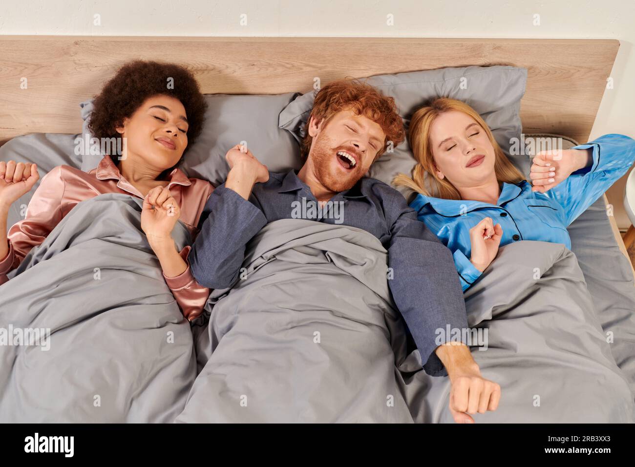 polyamory concept, three adults, man and interracial women in pajamas ...