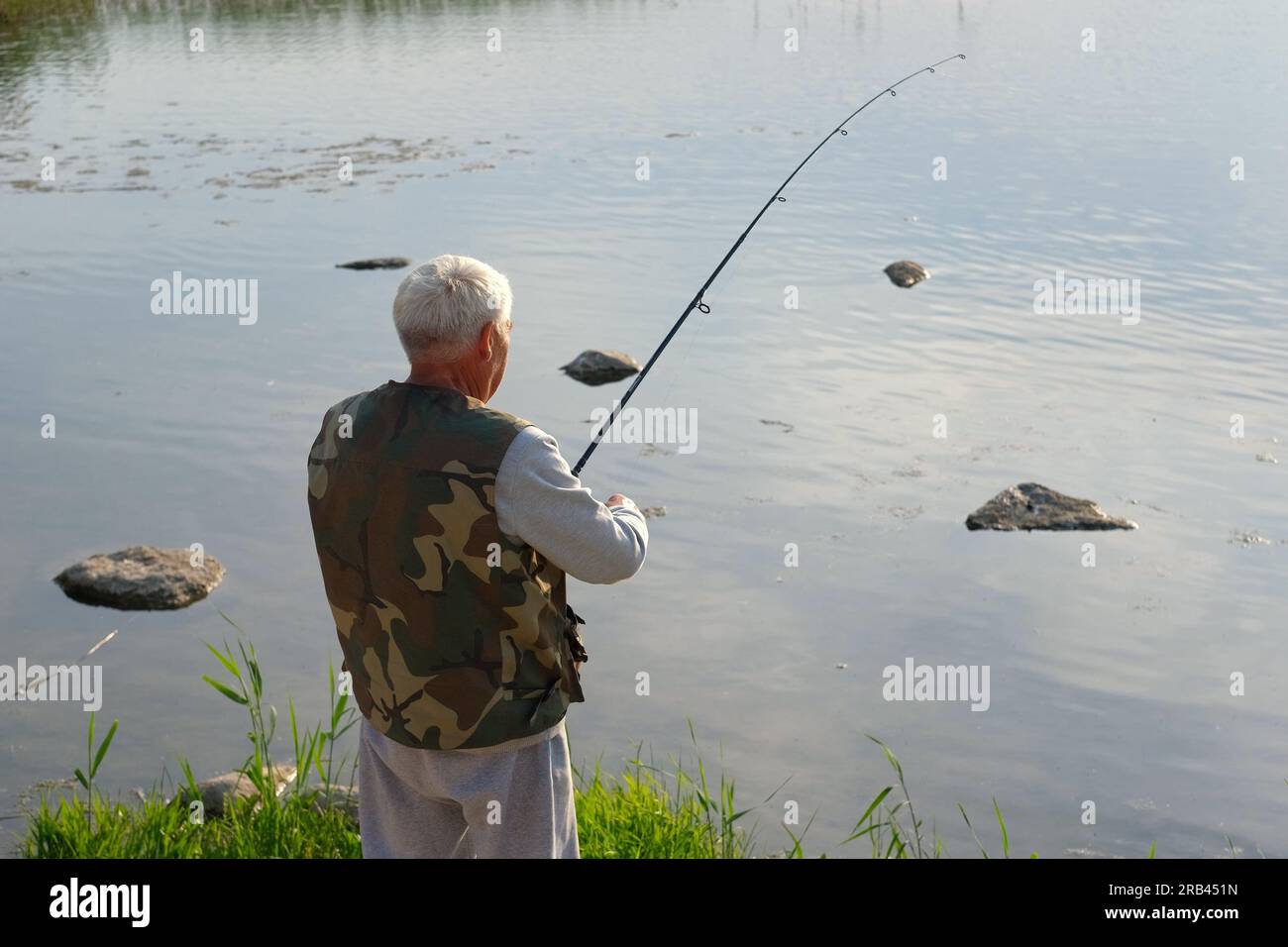 Old man fishing. Senior gray haired fisherman throws a spinning from ...
