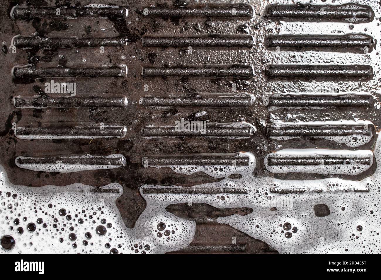 Cast iron grill pan with white detergent foam and water, abstract ...