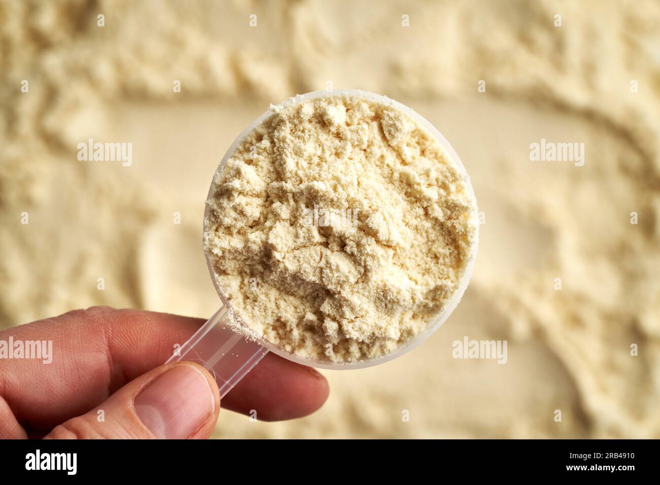 Hand holding a plastic measuring cup with whey protein powder, top view ...