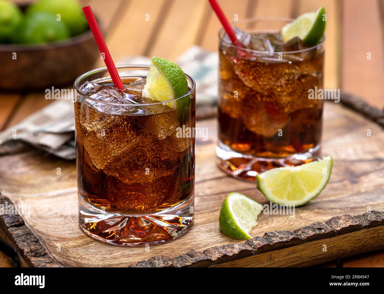 Rum and cola cocktail with ice and lime slices on rustic wooden tray ...