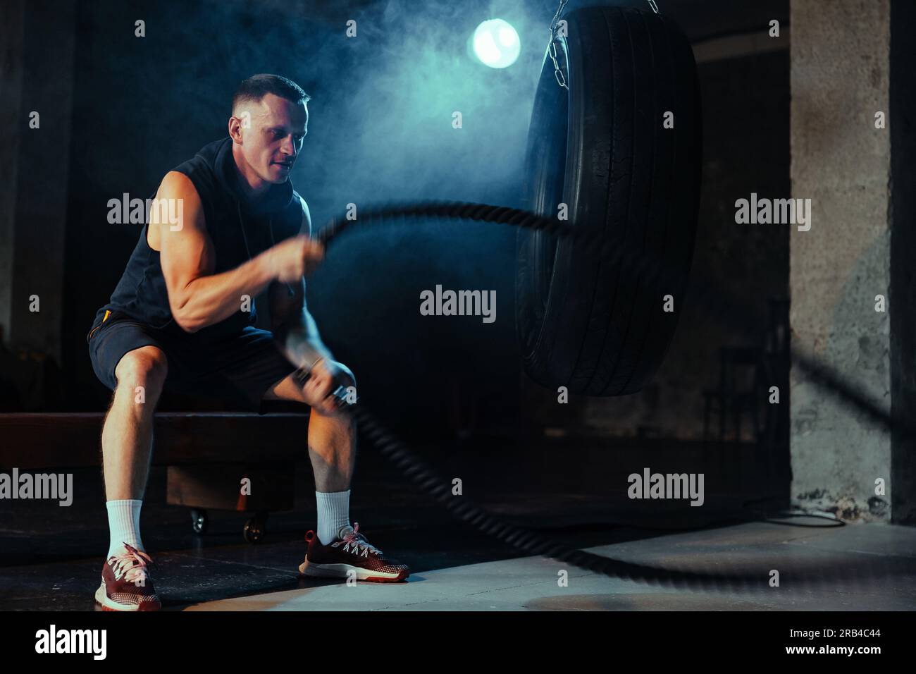 Strong muscular man exercising in dark gym with fighting ropes. Ropes ...