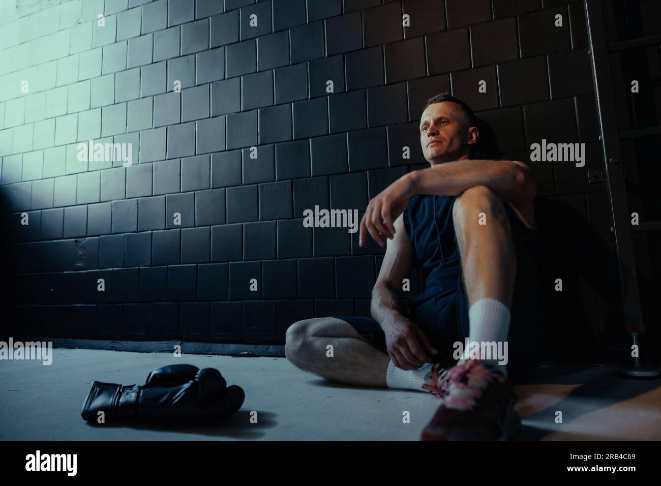 Tired boxer resting in dark gym after exercising near boxing gloves on ...