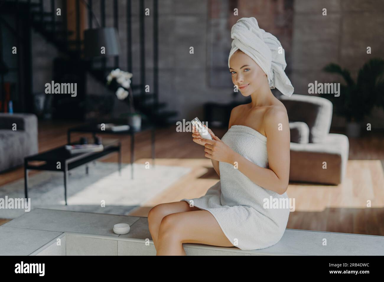 Lovely woman applies body lotion, glowing skin treatment. Cozy room ...